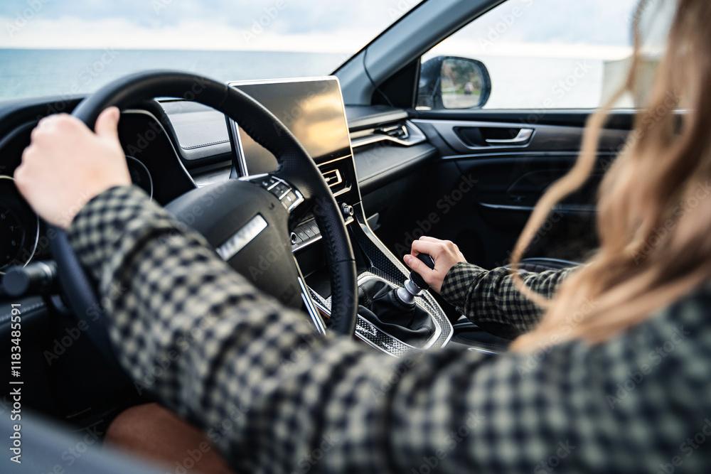 Back side view of an unrecognizable woman with long wavy hair driving a ...