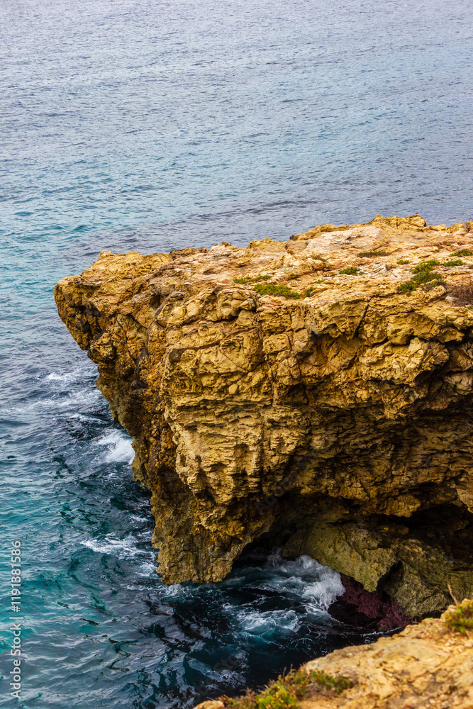 Rocky Coastal Cliff Overlooking Clear Blue Ocean with Small Structures ...