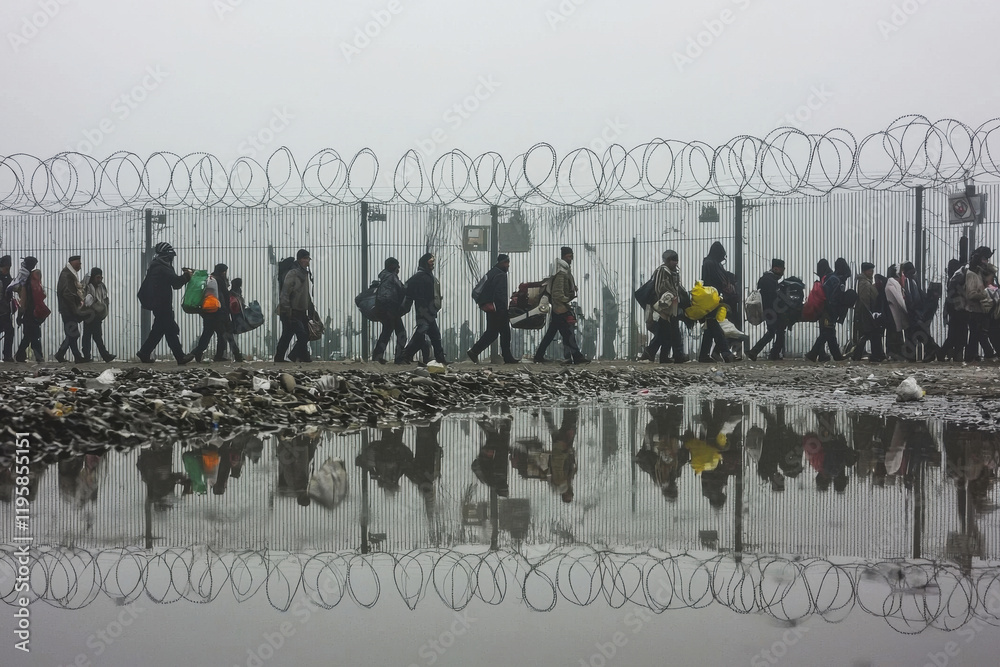 Refugees walking past barbed wire fence Stock Photo | Adobe Stock