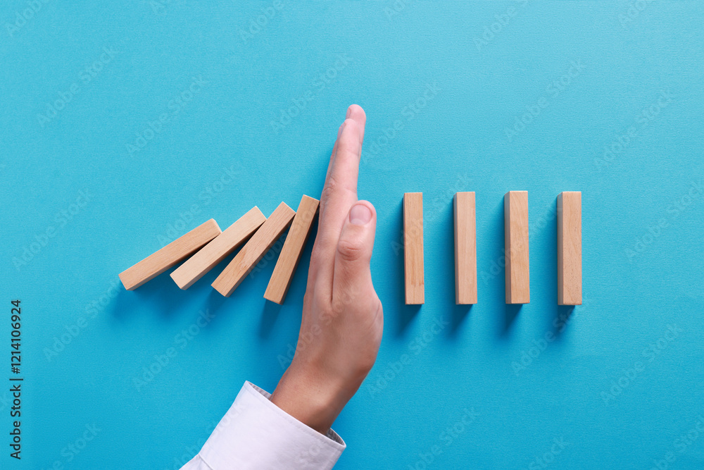 Man stopping wooden blocks from falling on light blue background, top ...