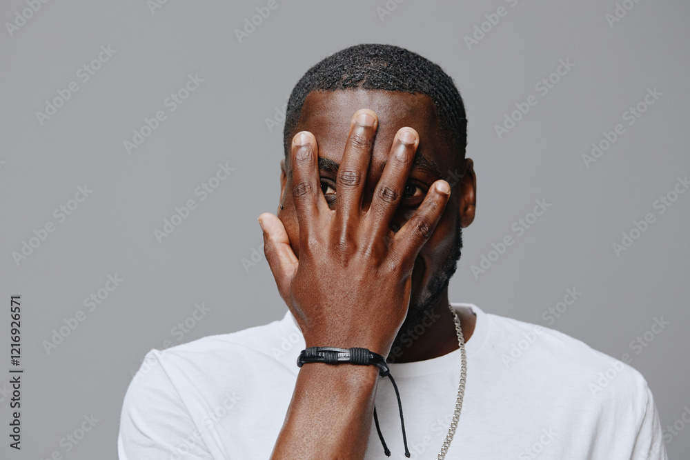 Portrait of a young man partially covering his face with his hand ...