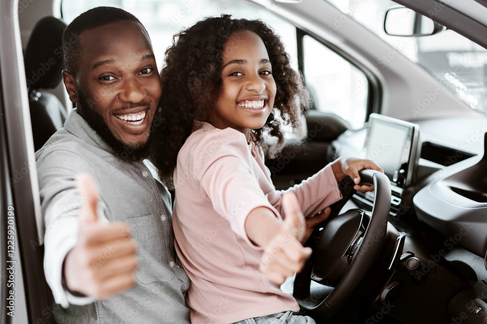 Happy black father and his daughter sitting on driver seat of new car ...