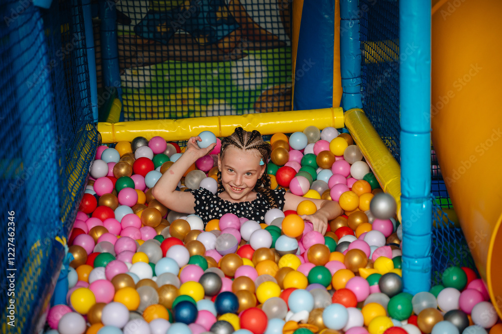 Young girl playing in a colorful ball pit at an indoor play center ...