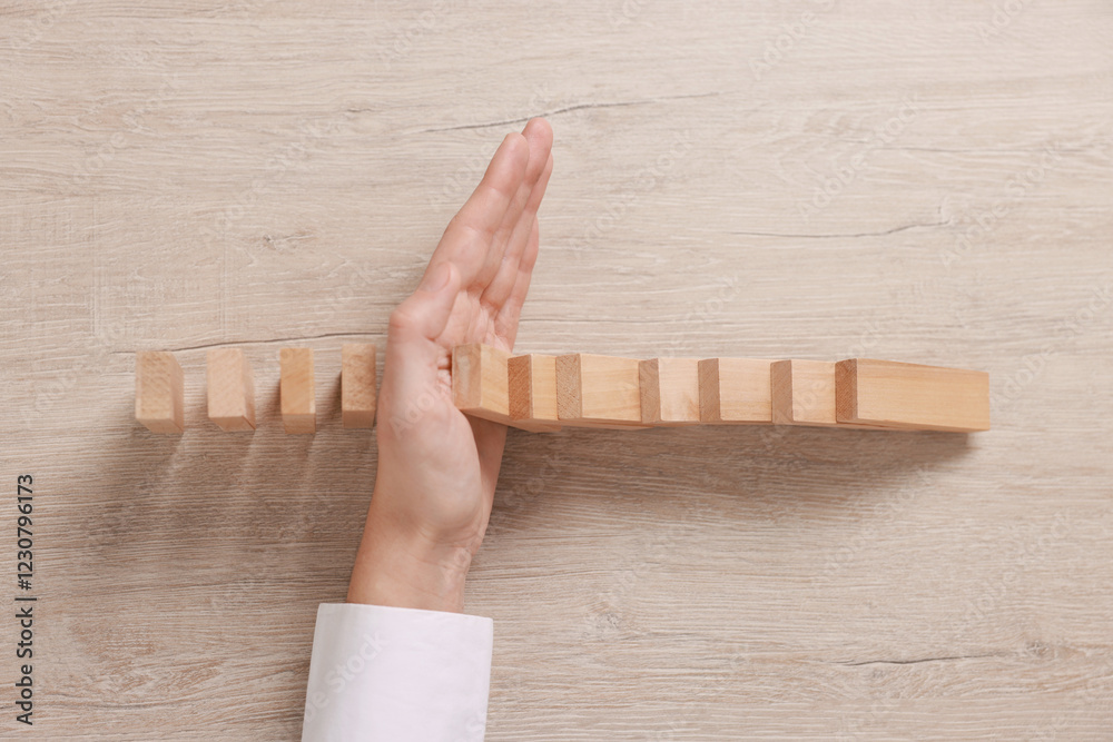 Woman stopping wooden blocks from falling at table, closeup. Domino ...