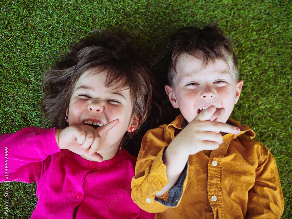 Joyful twin siblings playfully lying on grass while sharing a secret in ...