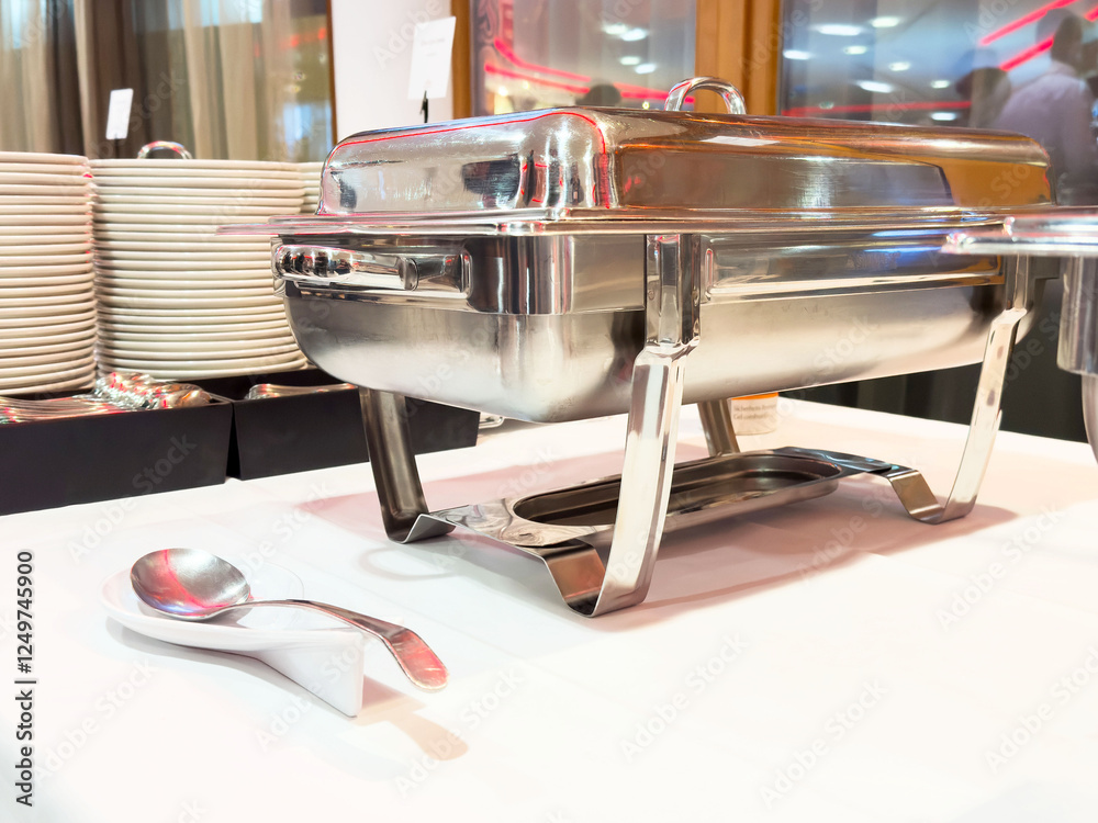 Shiny stainless steel chafing dish on buffet table with plates and ...