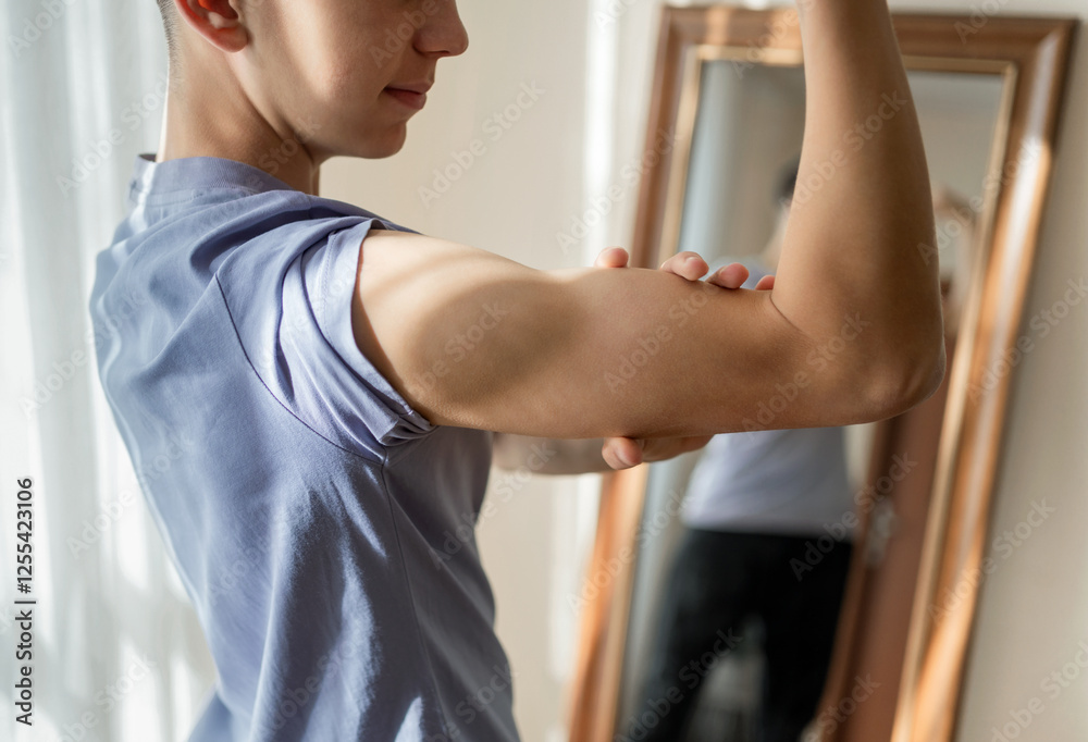Teenage boy checking degree of muscle pumping on his arm in front of ...