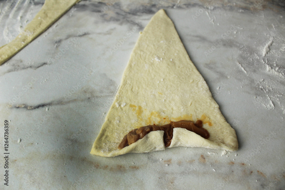 Triangle of raw dough with filling boiled condensed milk close-up view ...