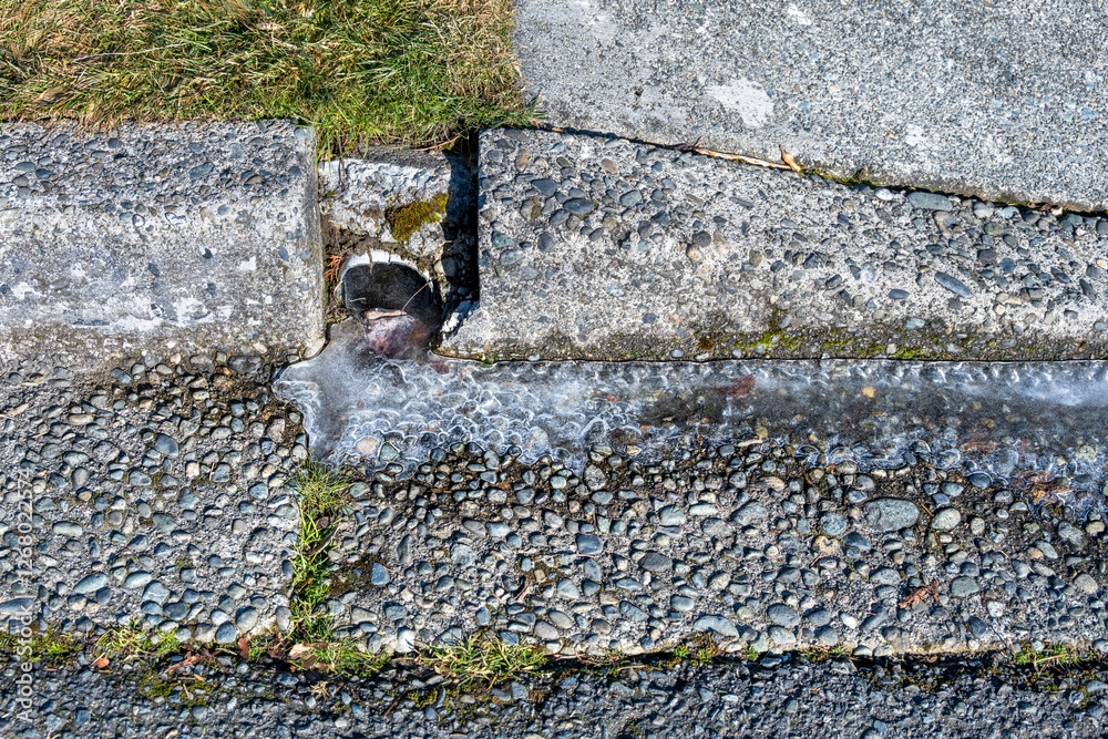 Stormwater outflow from residential yard on a frozen sunny winter day ...