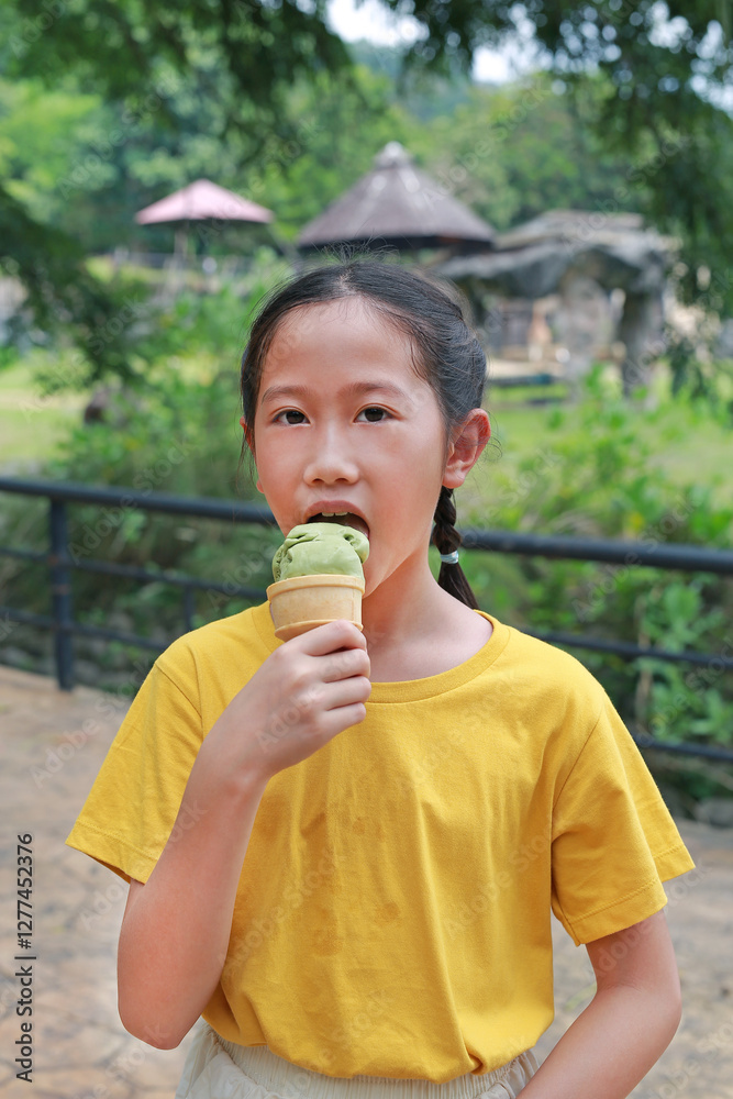 Asian young girl child eating tasty green tea ice cream in the garden ...