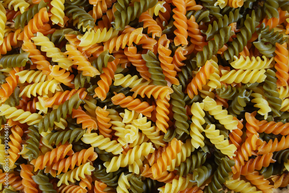 raw tricolor spiral-shaped pasta (Fusilli), spread out on a surface and ...