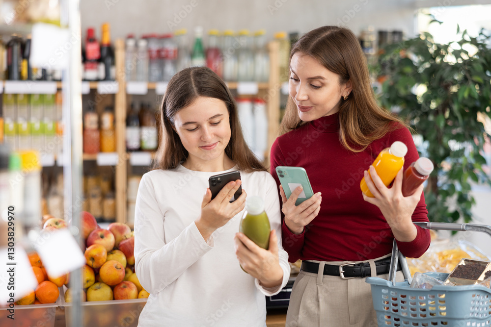 Attentive teen girl and her mom checking QR-code on bottle of smoothie ...
