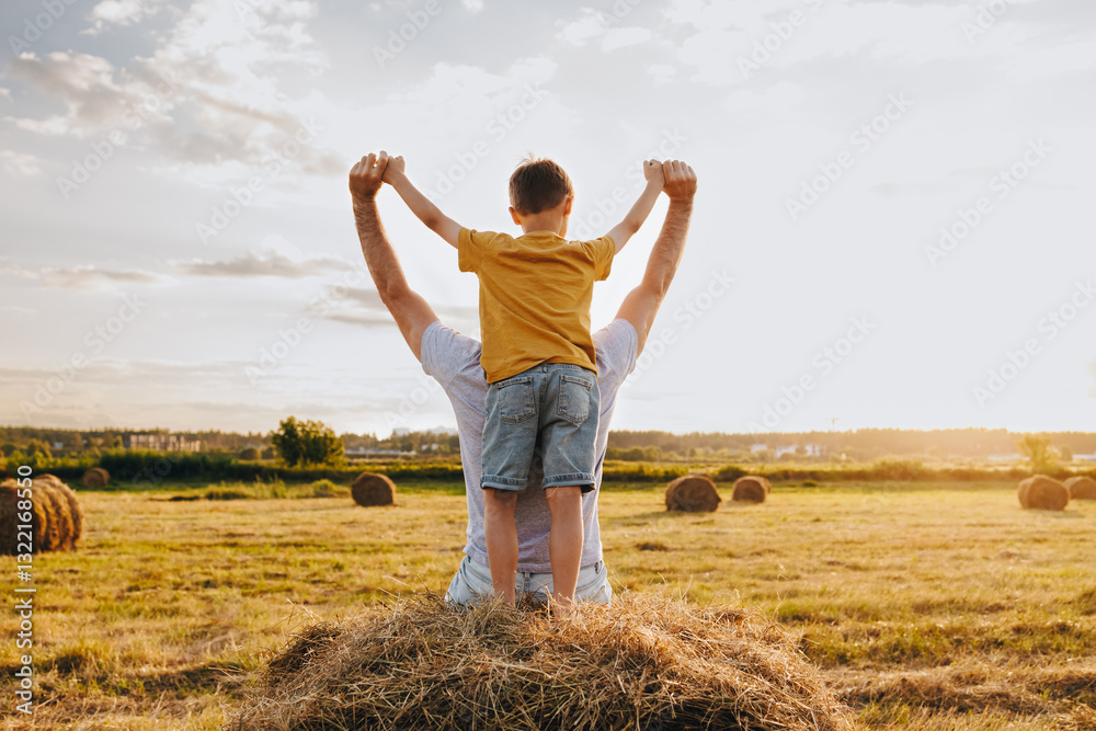 Father holding his son on his shoulders in a sunlit field, raising ...
