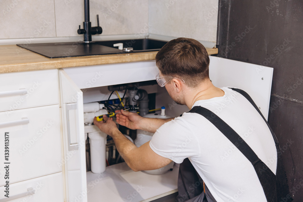 Plumber installing water filter using screwdriver in kitchen sink ...