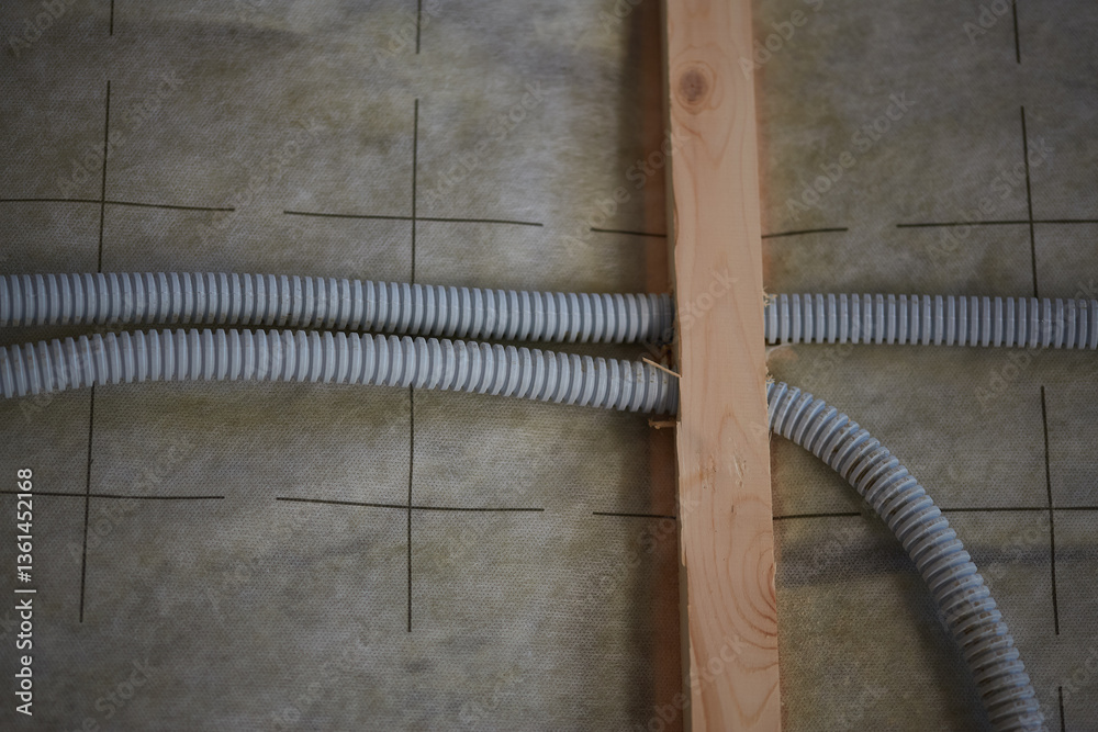 Electrical conduits are installed along wooden beams against a textured ...