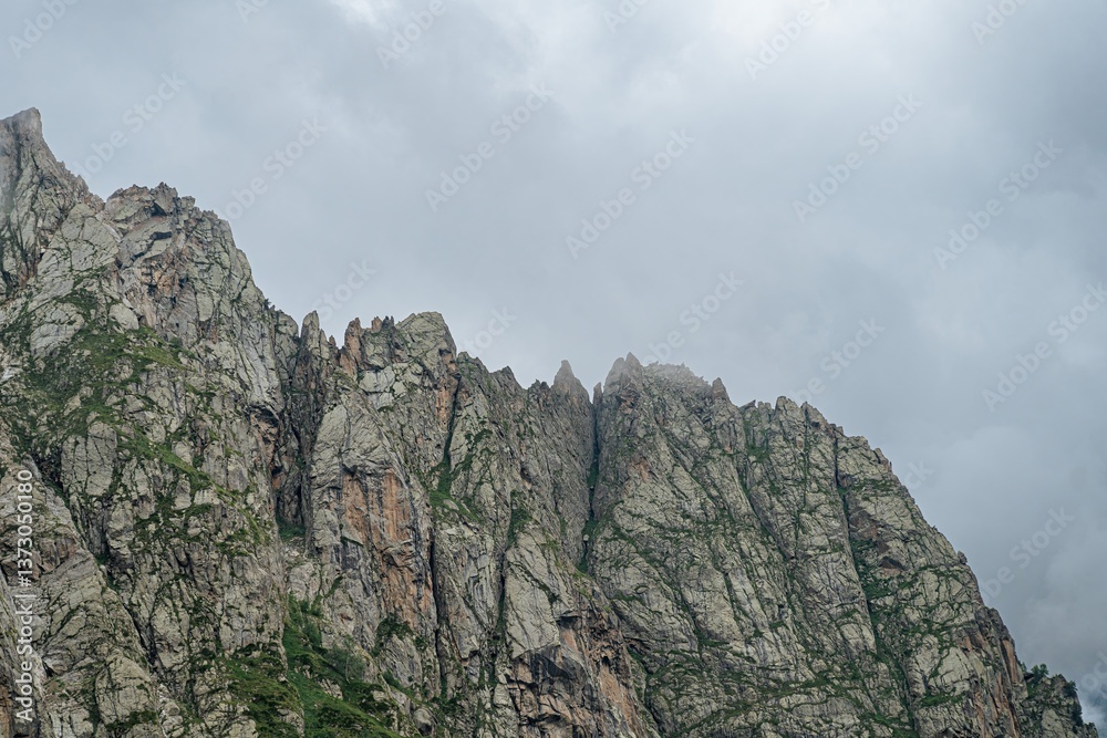 Towering mountain ridges stand tall under a moody sky, their rugged ...