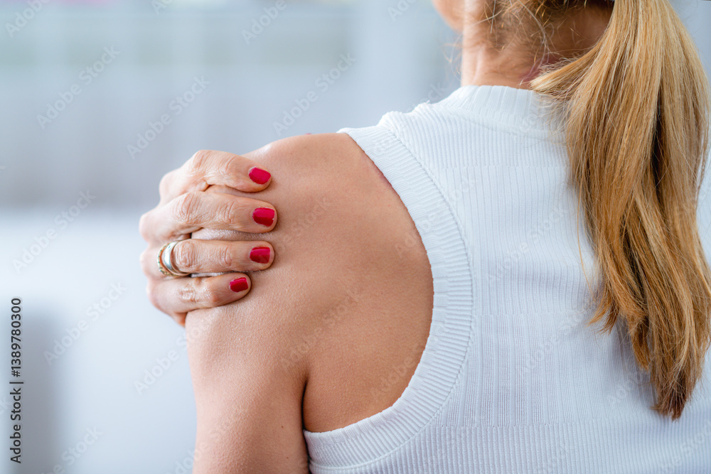 Woman experiencing shoulder pain, holding her sore shoulder with ...