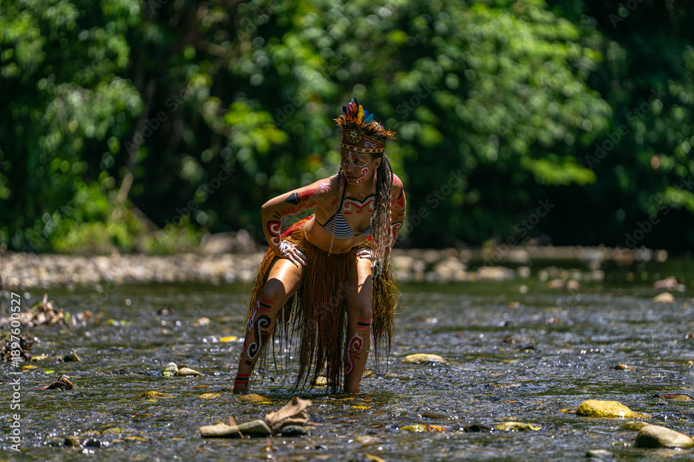 Indigenous woman crouches in a shallow river wearing tribal attire and ...