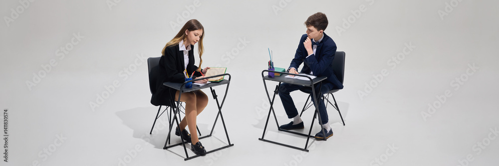 Two students, boy and girl in school uniforms, sitting at desk and ...