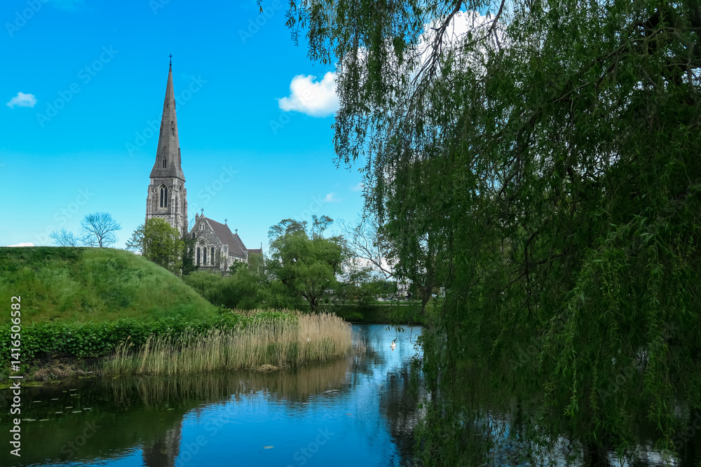 St. Alban's Church reflects beautifully in calm blue water of moat ...