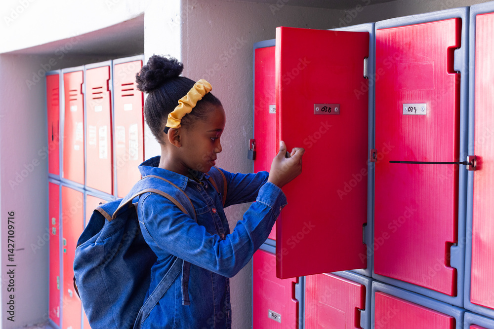 African American child reaching into red locker door in school hall ...