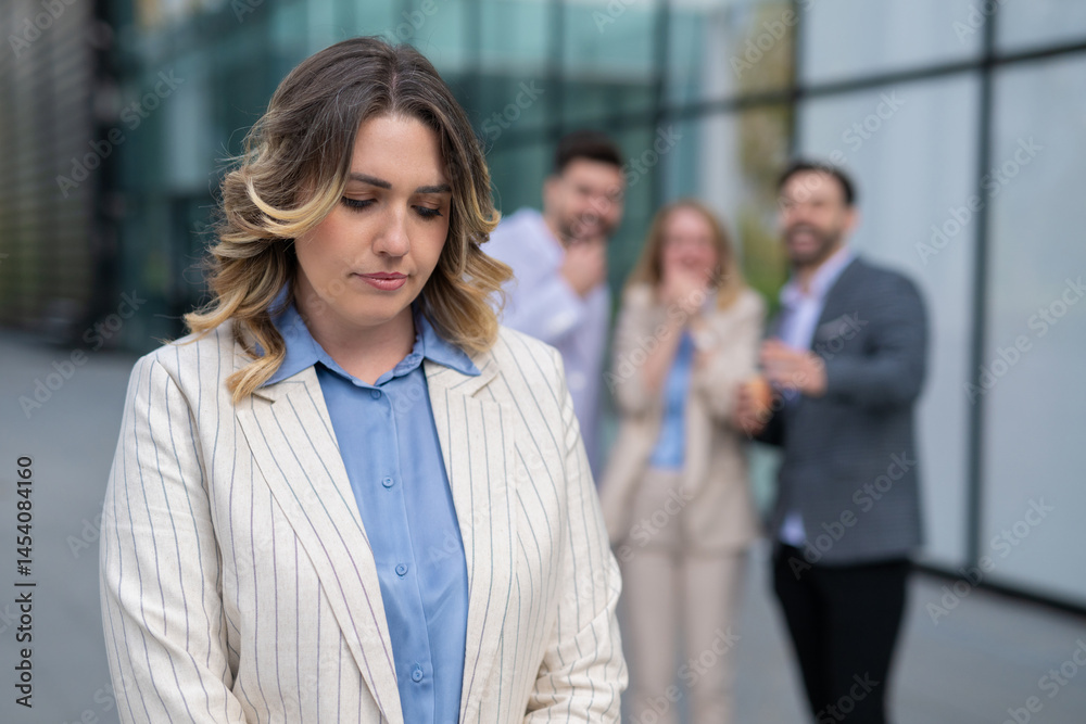 Sad businesswoman facing bullying at work while coworkers laugh behind ...