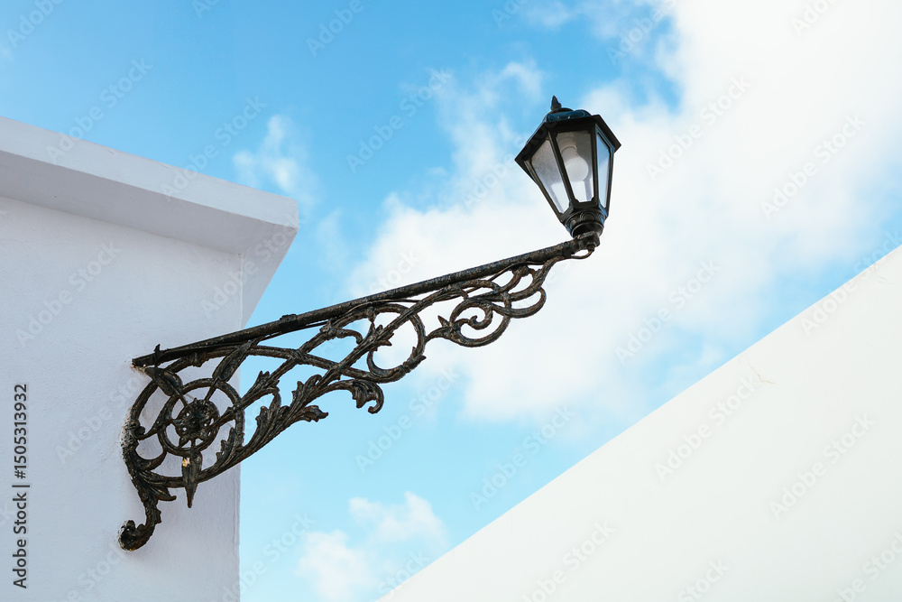 Ornate wrought iron lantern bracket on a whitewashed building in Plaka village, Milos island ...