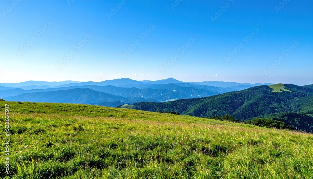 Rolling green hills slope to distant blue mountain ranges under a clear ...