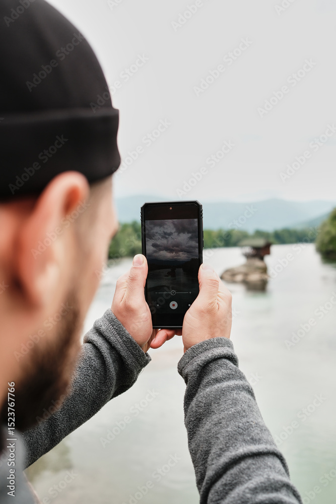Close-up of a man filming the Drina River house on his phone, capturing ...