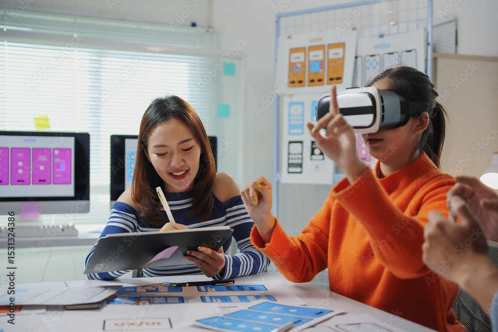 Asian women engaging in testing a virtual reality app and taking notes ...
