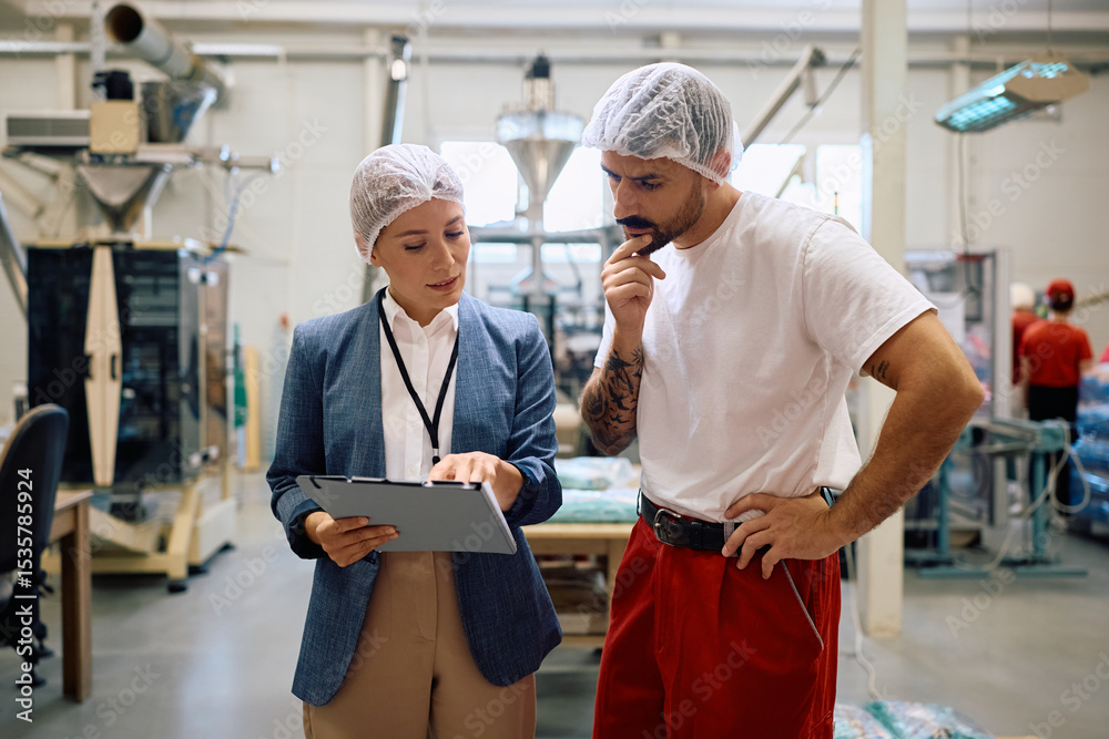 Female manager and employee going through paperwork at factory plant ...