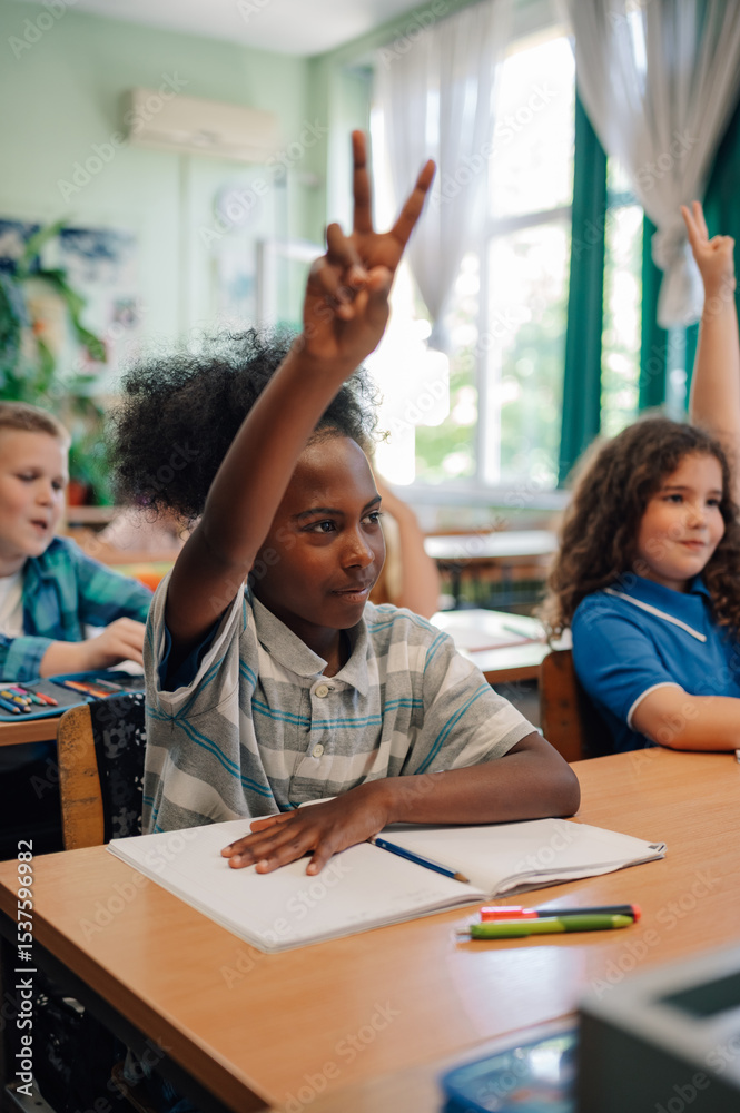 Elementary school student raising hand showing peace sign in classroom ...
