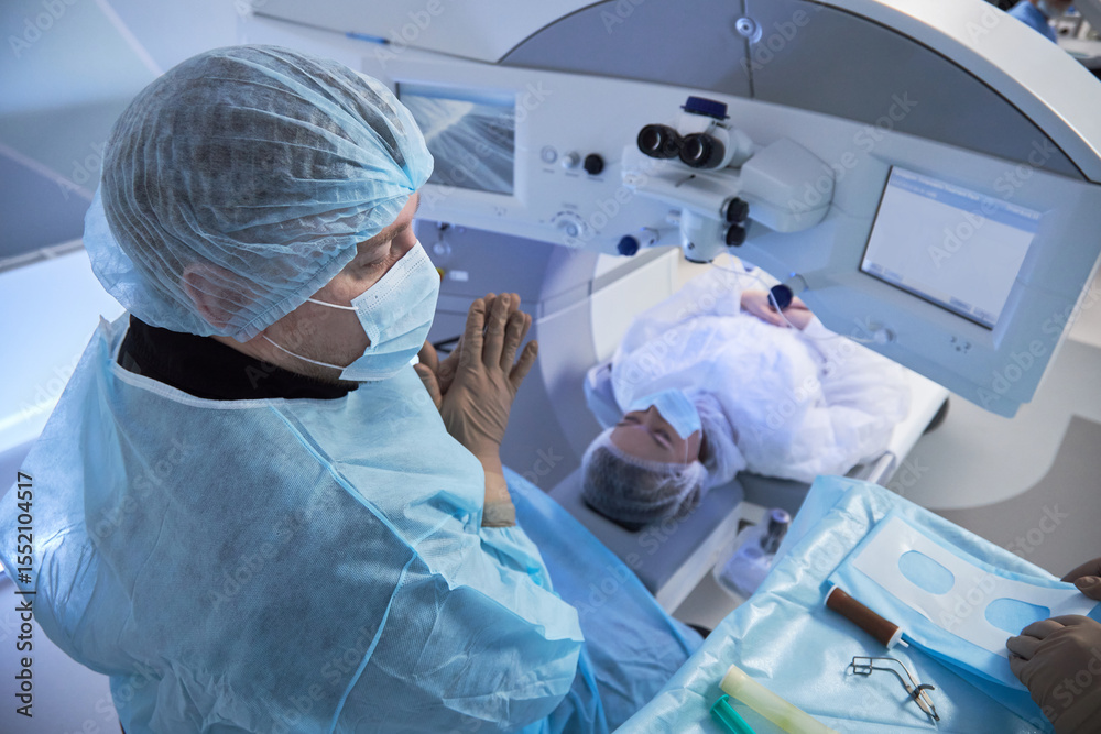 Middle aged male surgeon preparing for eye surgery on woman lying under ...