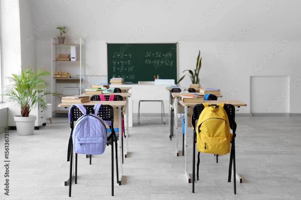 Interior of light classroom with desks, backpacks on chairs and ...