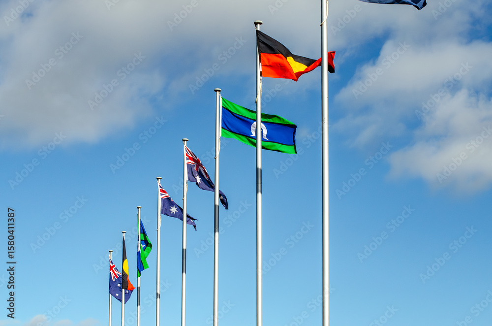 A row of flags flying high against sky in Australia, including the ...