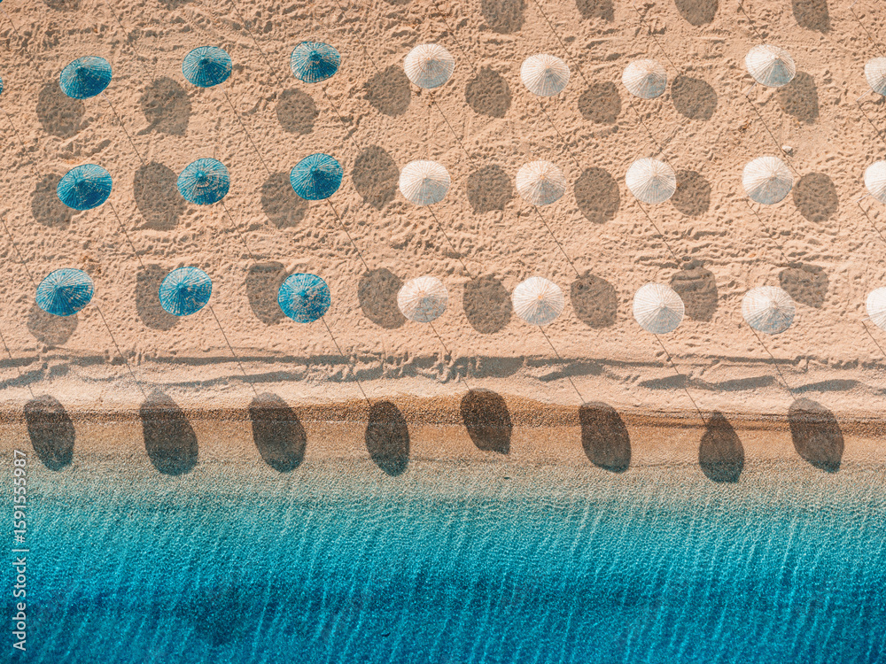 Aerial view of rows of beach umbrellas and deckchairs casting shadows ...