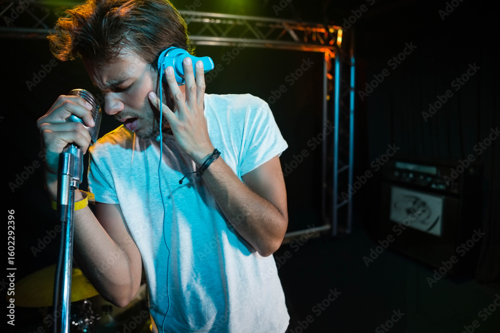 Singer wearing white tee, blue headphones, gripping mic under metal ...