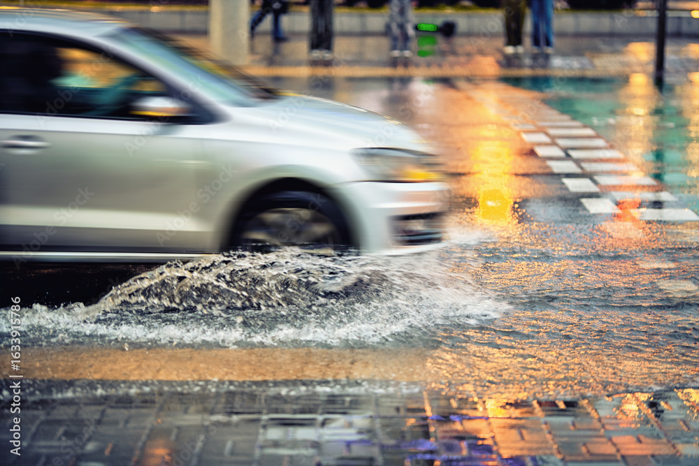Car wheel splashes large puddle at pedestrian crossing in the evening ...