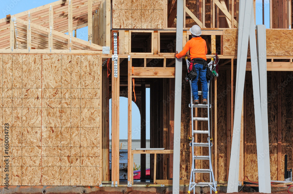 A construction worker wearing safety gear stands on a ladder while ...
