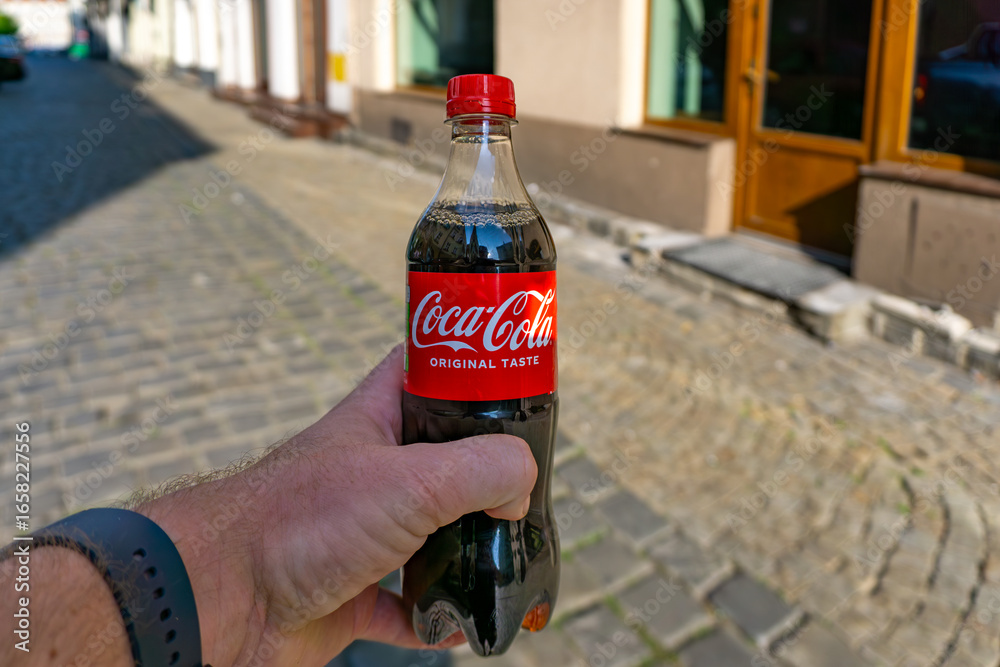 Hand holding Coca-Cola Original Taste plastic bottle on cobblestone ...