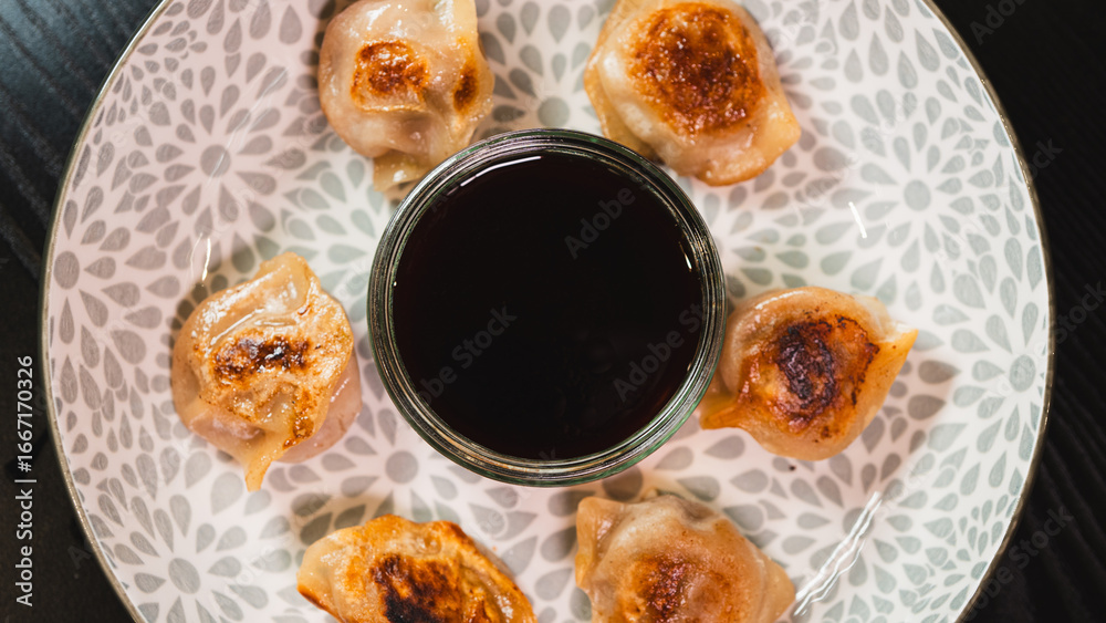 Golden-brown pan-fried dumplings presented on a stylish plate with a ...