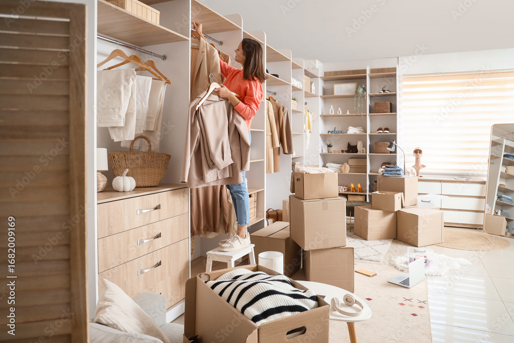 Young woman taking clothes from rack with wardrobe boxes in dressing ...