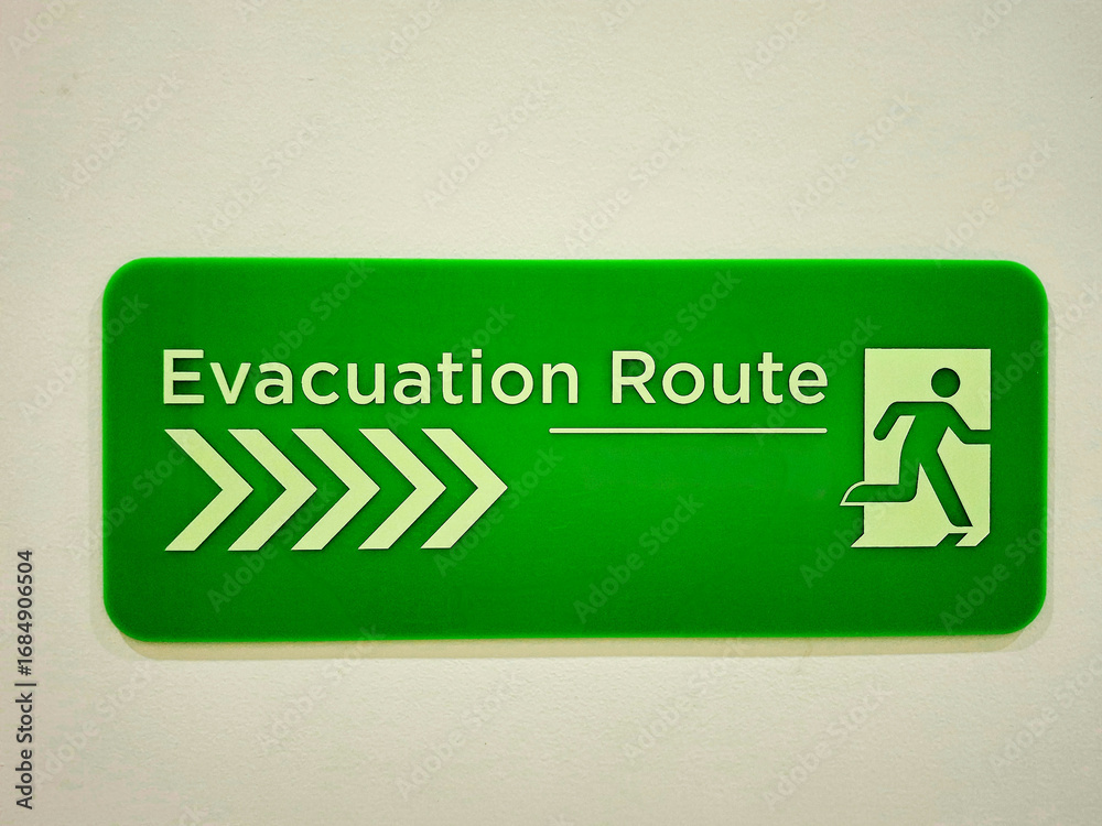 Green emergency evacuation route sign on wall with arrow and running ...