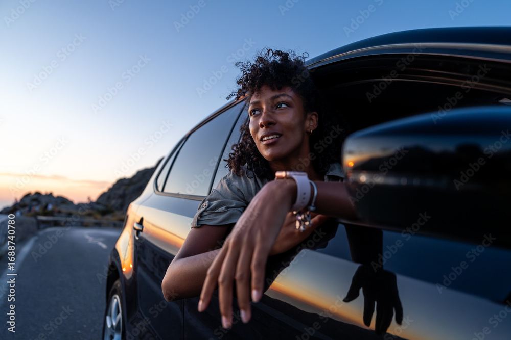 Young woman enjoys golden hour scenery from car window. Concept of ...