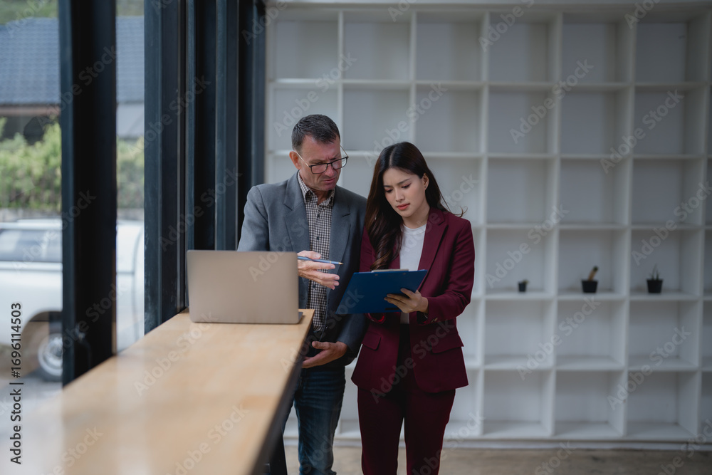 Businesspeople discussing work using laptop and clipboard, senior ...