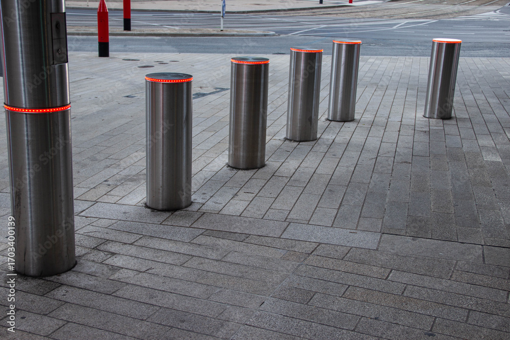 Metallic bollards with illuminated tops line a modern urban sidewalk ...