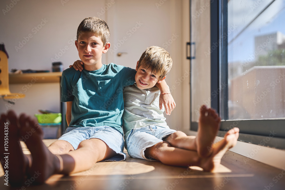 Brothers sitting on floor indoors with arms around each other, siblings ...