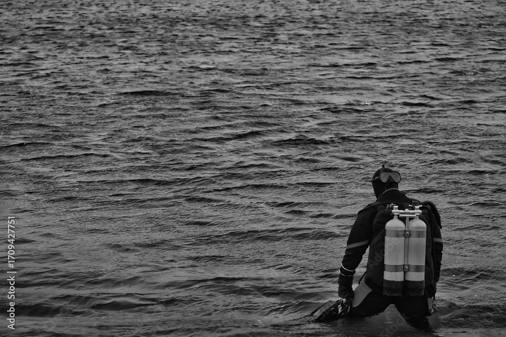 Diver in a dry suit prepares to dive into cold water, extreme diving ...