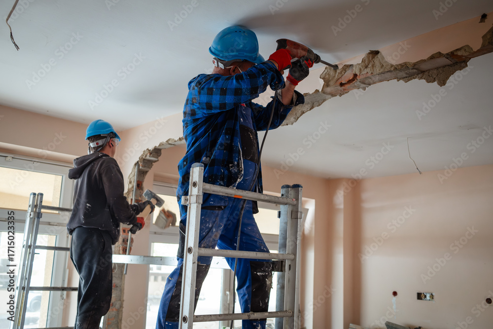Two construction workers on scaffolding demolishes a wall in a building ...