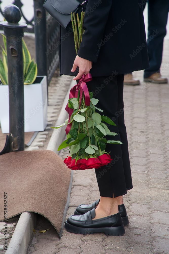 Unrecognizable young woman in black holds a bouquet of red roses during ...